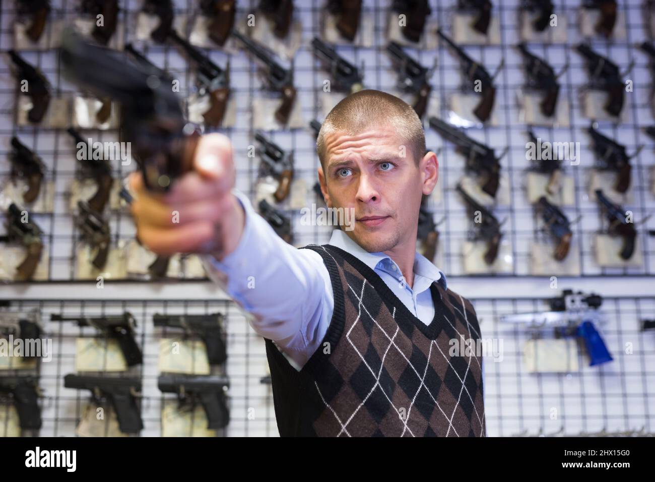 Focused man testing pistol aiming in armory shop Stock Photo - Alamy