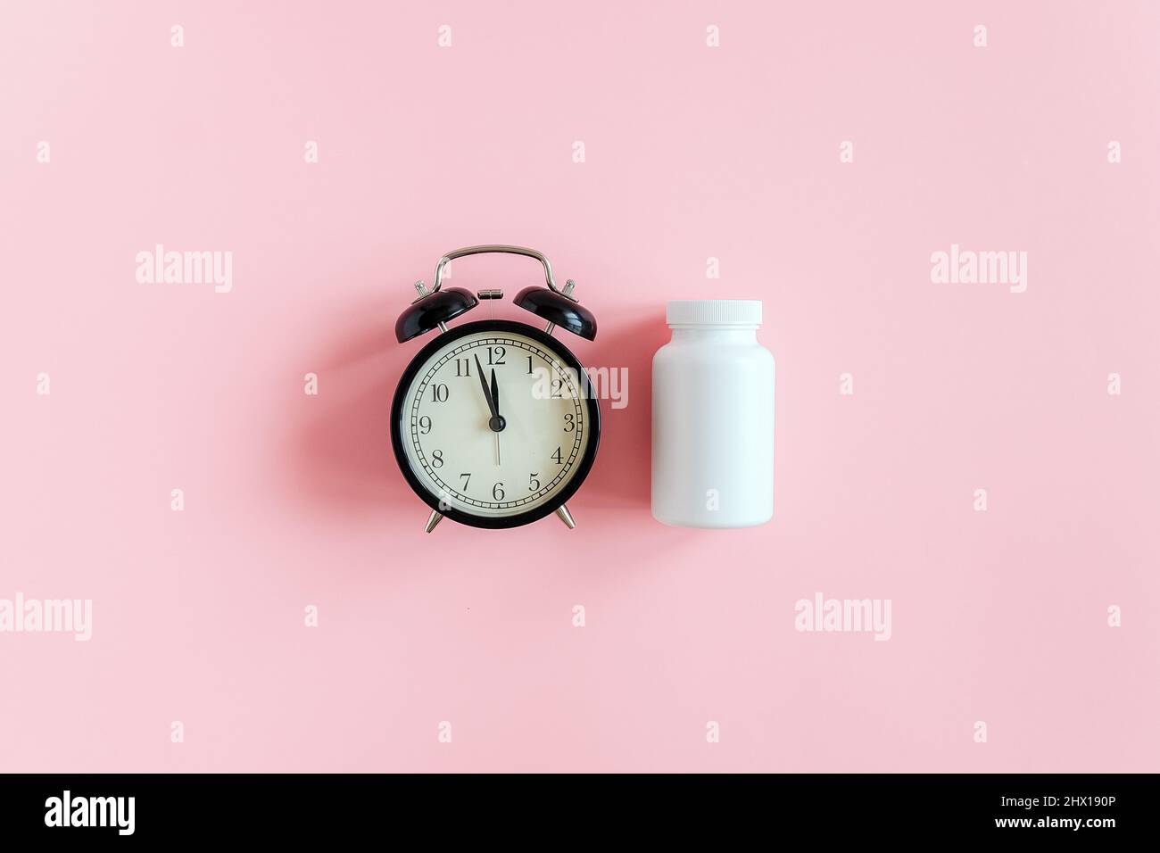 White medical bottle with pills and black alarm clock on pink ...