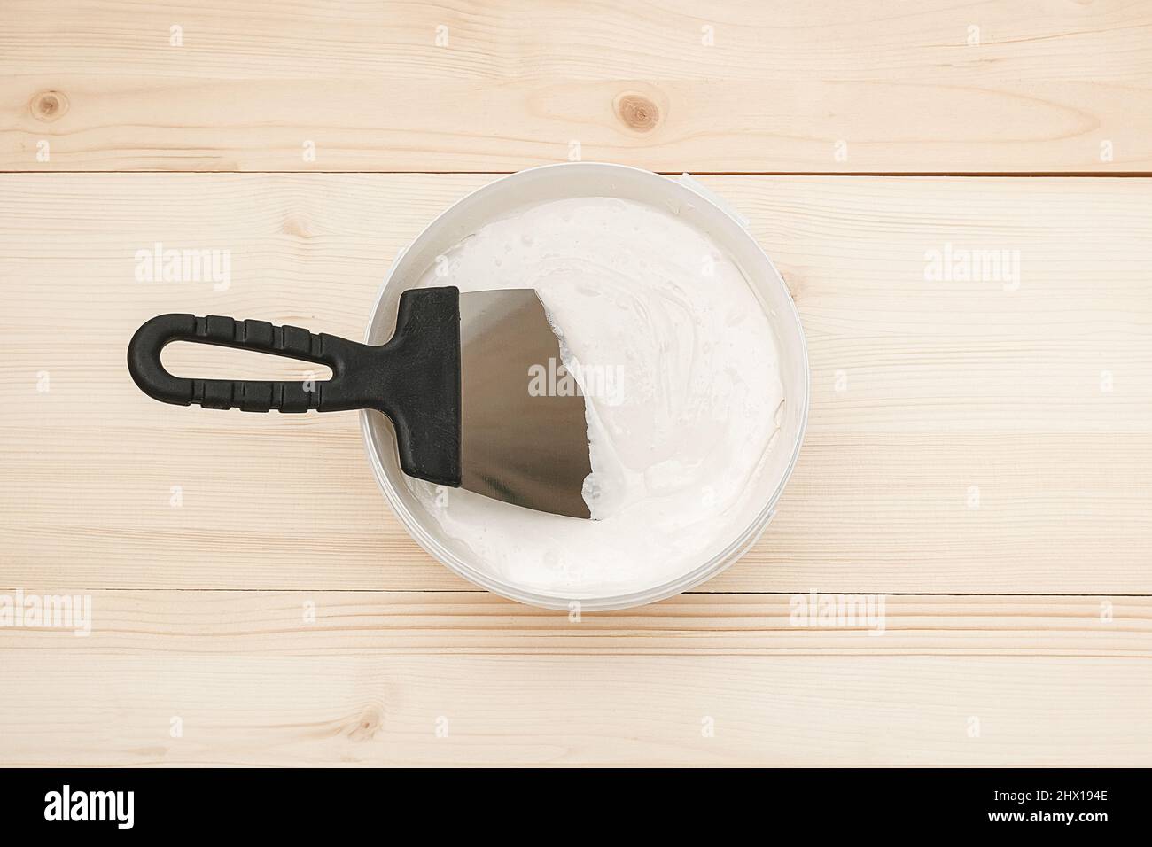 Spatula and a bucket of white putty on wooden boards. Top view Copy ...