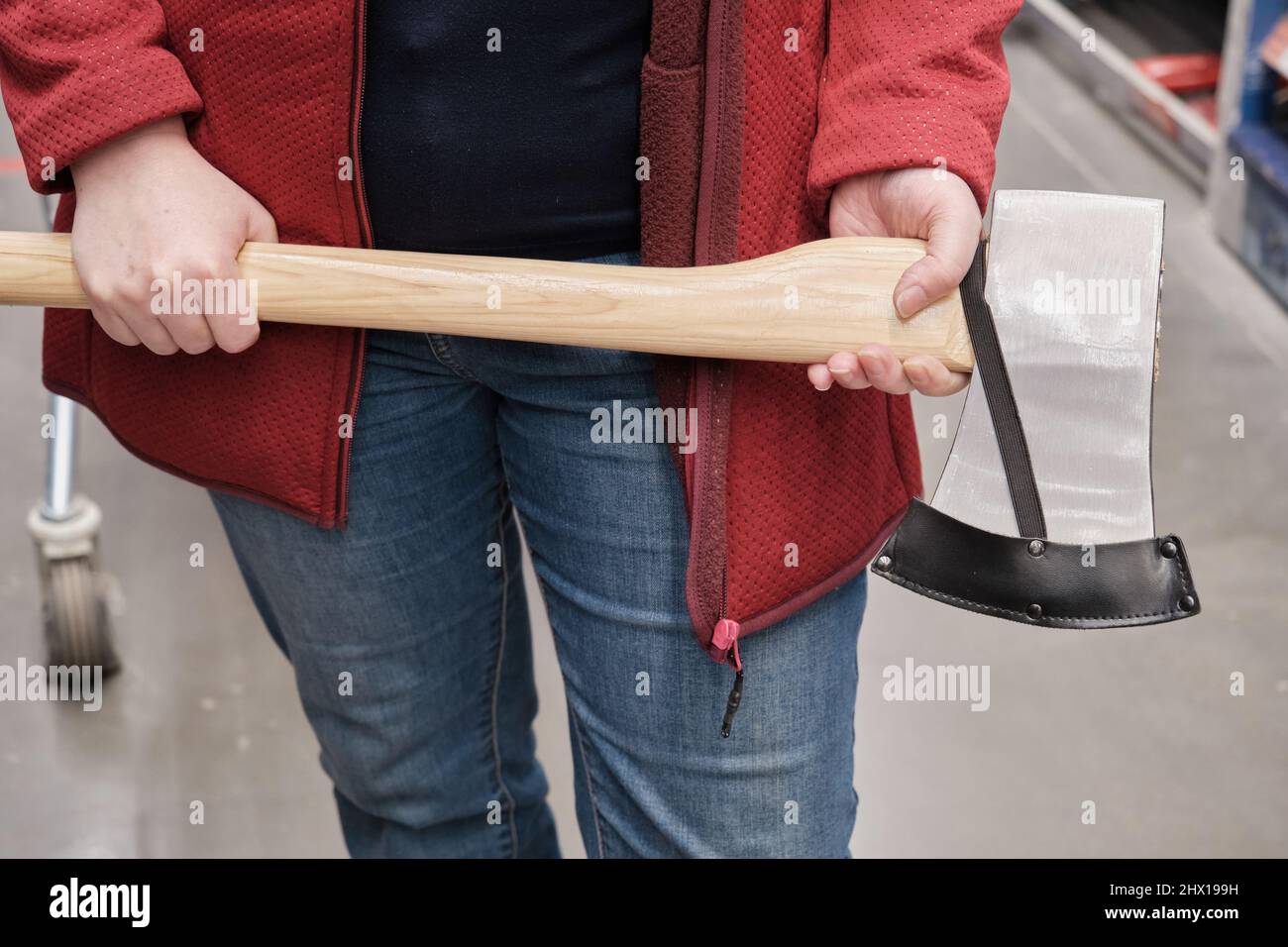 Woman in building materials store chooses for buy big axe. Hands close ...