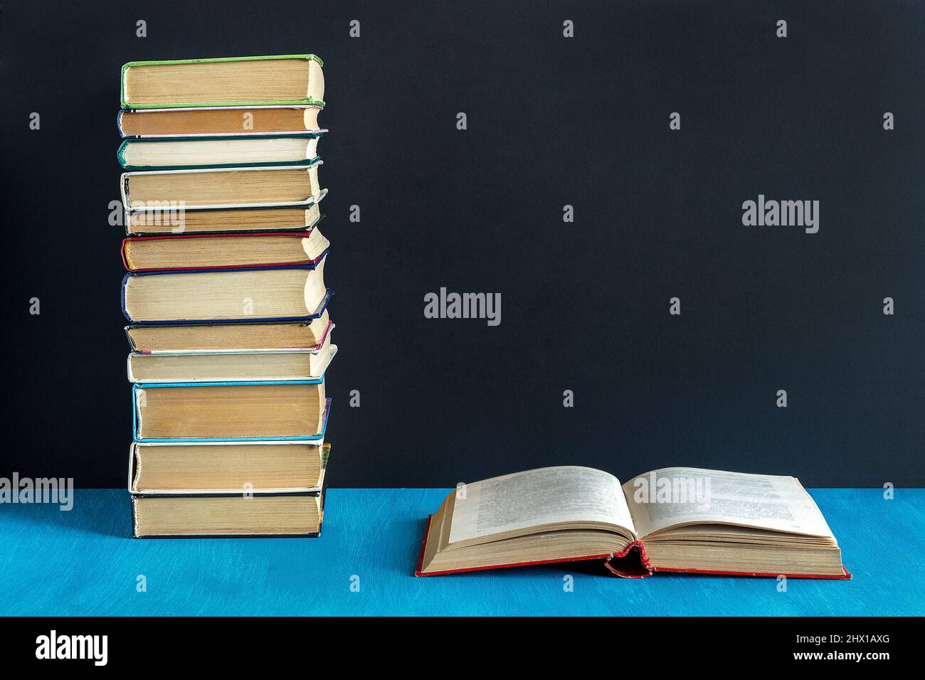 Open book, stack of books on blue table on black chalkboard background ...