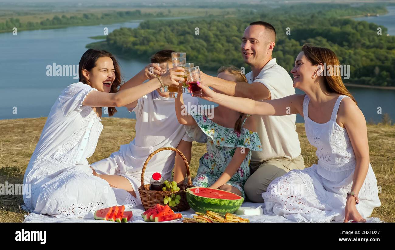 Parents with children clink glasses of soft drinks at picnic Stock ...