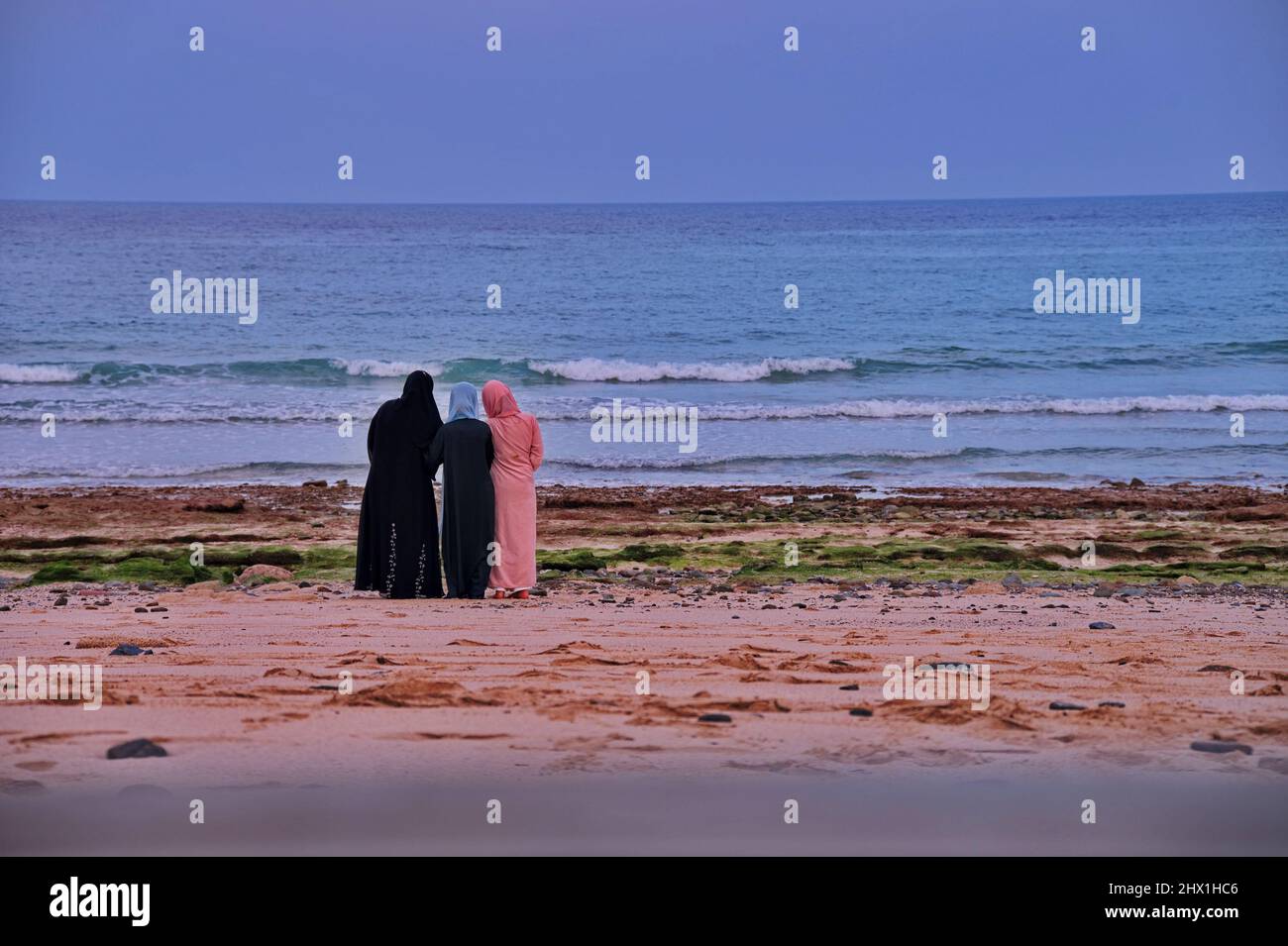 Rear view of three women in tradition arabian clothes at the sandy ...
