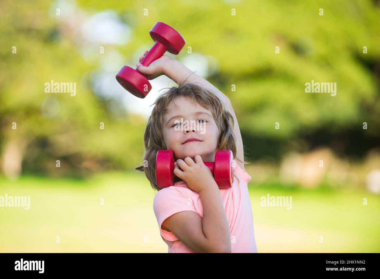 Child boy is doing exercises with dumbbells in summer park. Healthy ...