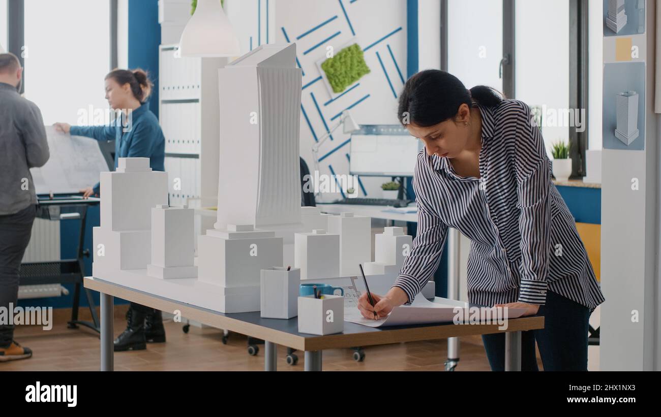 Woman Architect Analyzing Blueprints Plan On Table To Design Building Model And Maquette
