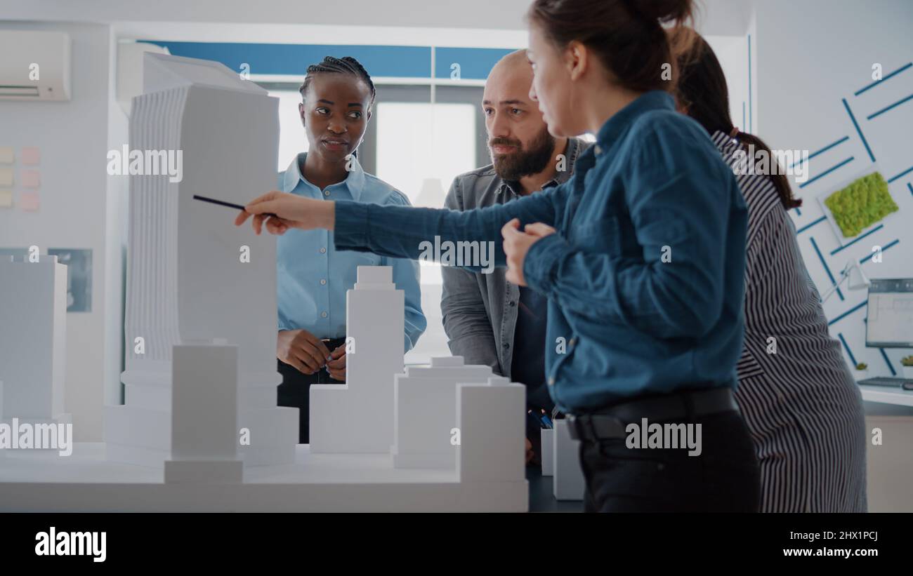 Team Of Architects Analyzing Building Model To Plan Construction Layout And Blueprints On Paper
