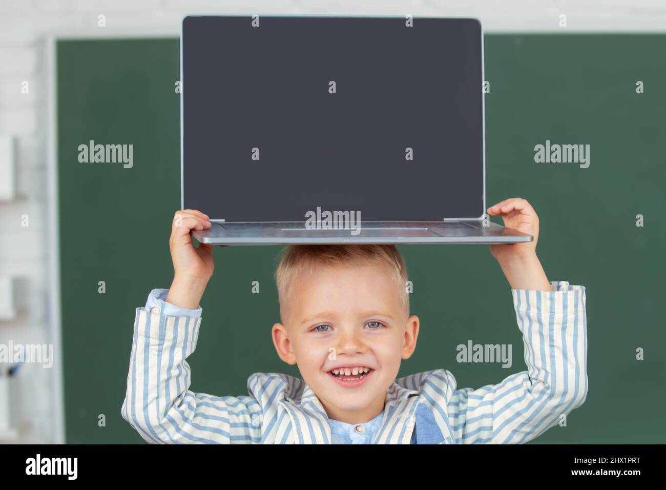 Close up portrait of child holding laptop on head, gadgets to study. Computer education for kids ...