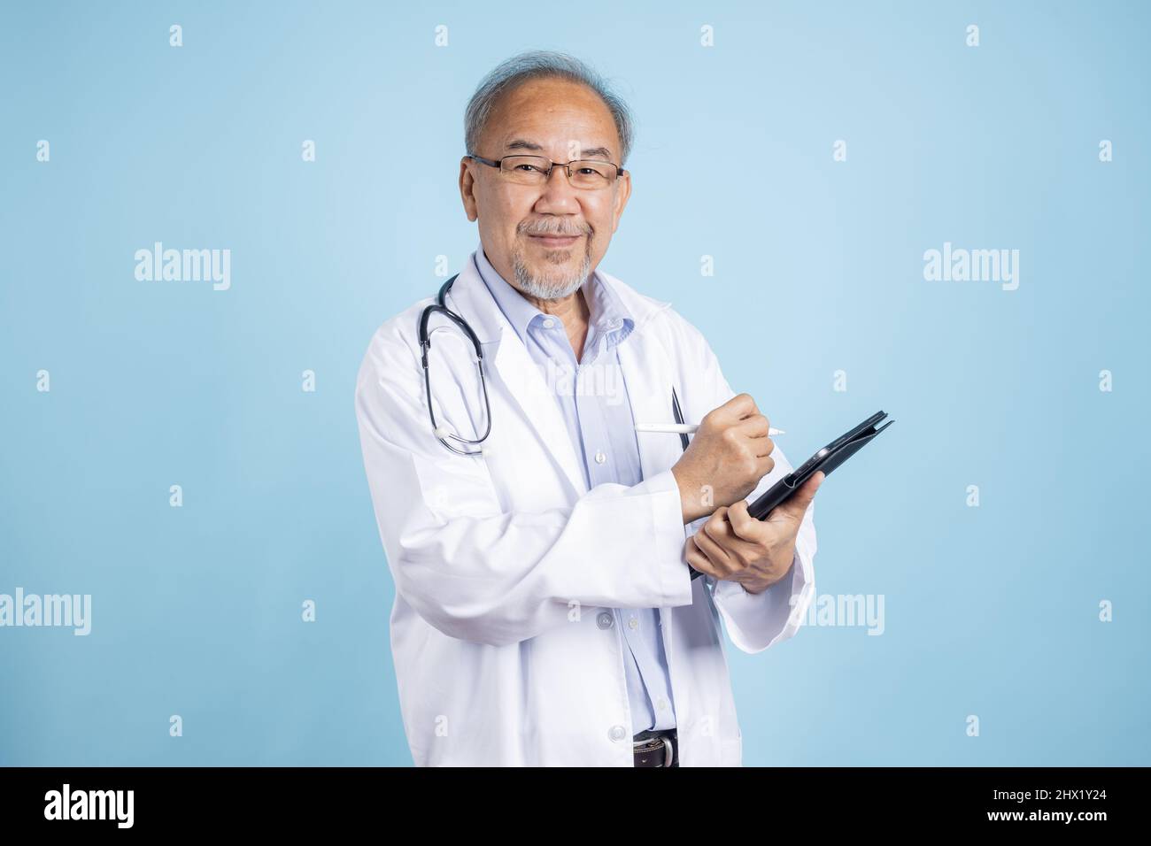 old man doctor holding tablet and smaile isolated on blue background ...