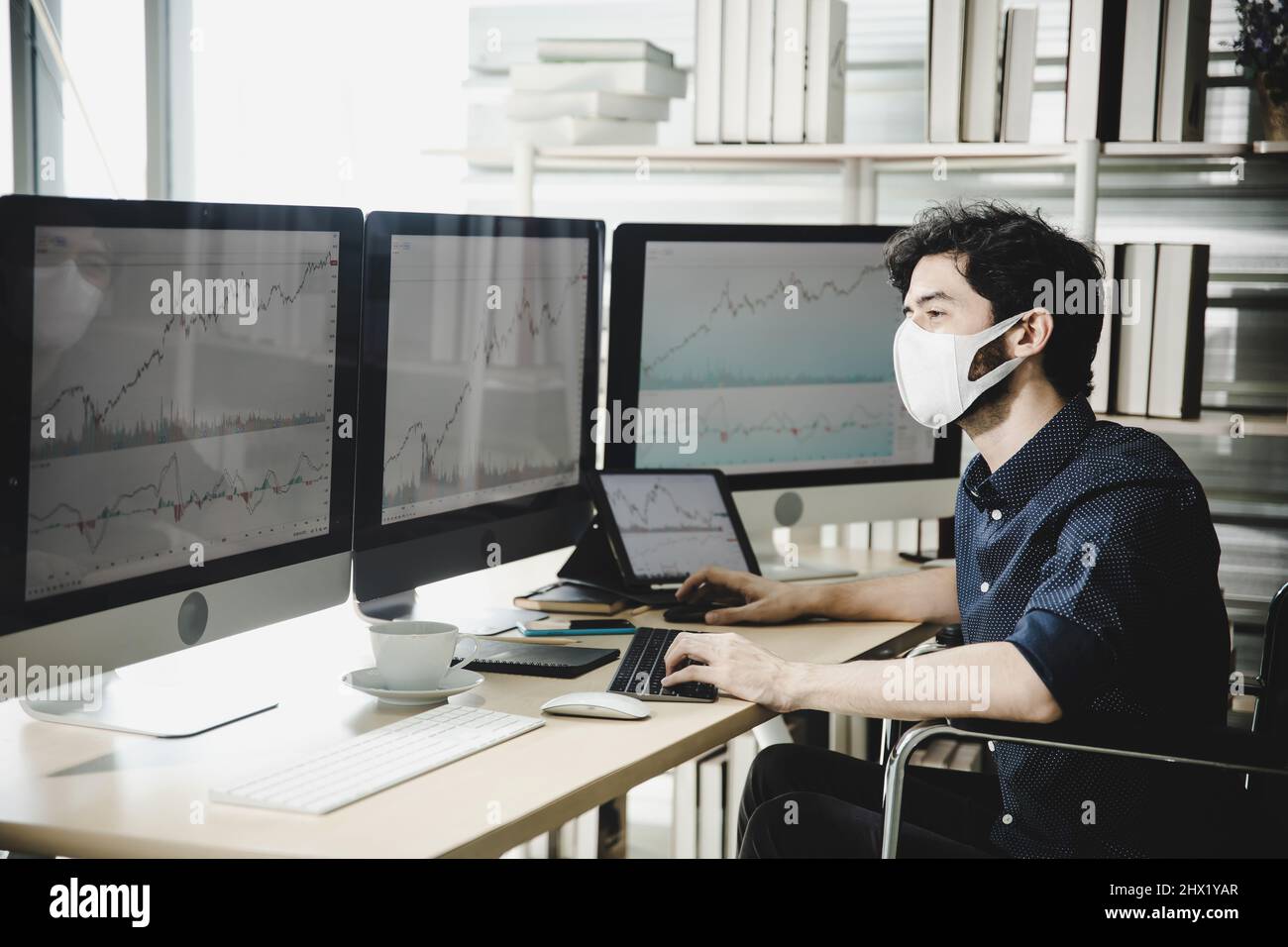 A businessman wears face mask and checks stock market data on monitor ...