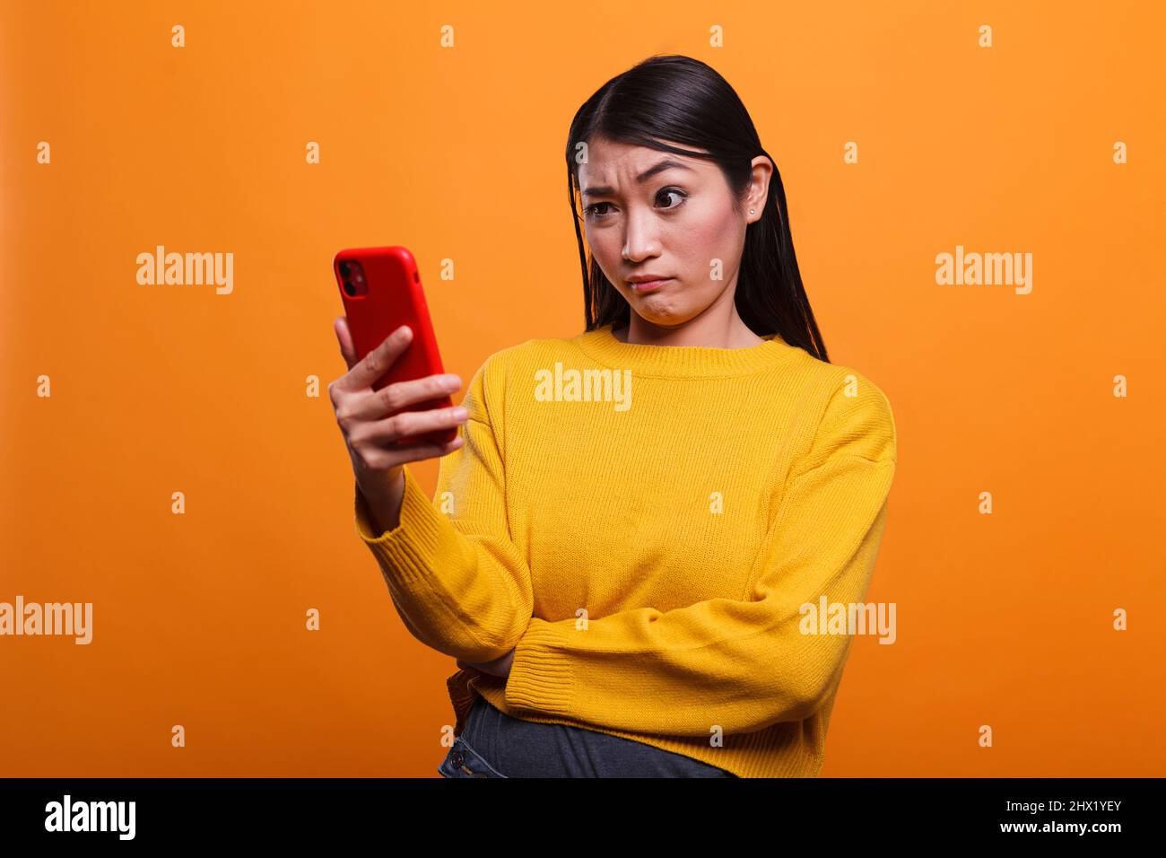 Doubtful uncertain beautiful woman wearing yellow sweater while using ...