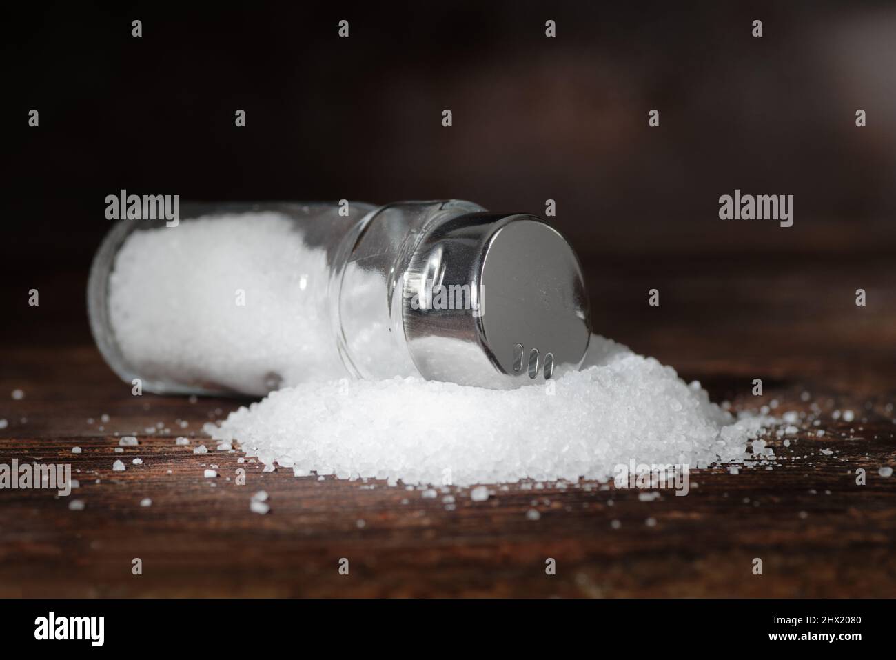 Salt from a salt shaker on wooden background. The concept of excessive ...