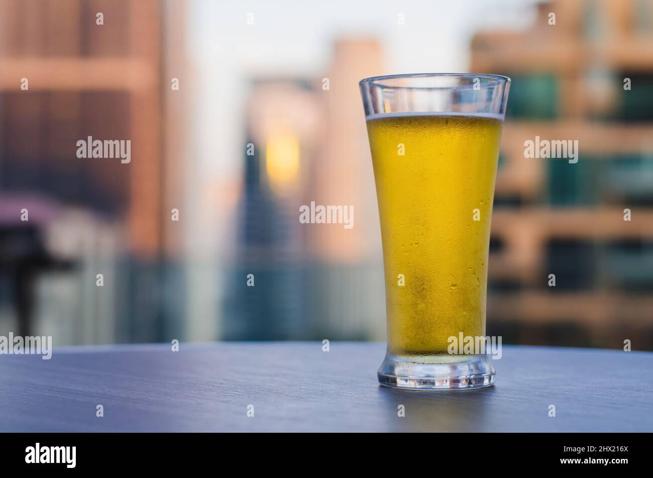 A glass of beer puts on table at rooftop bar with blurred city ...