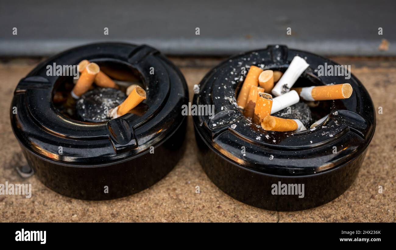 Cigarette in ashtray. Cigarette ends in two black ashtrays. Bad habit ...