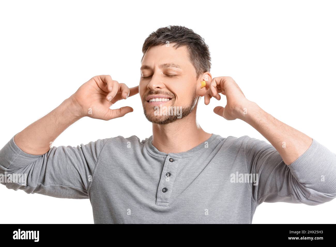 Handsome man putting yellow ear plugs on white background Stock Photo ...