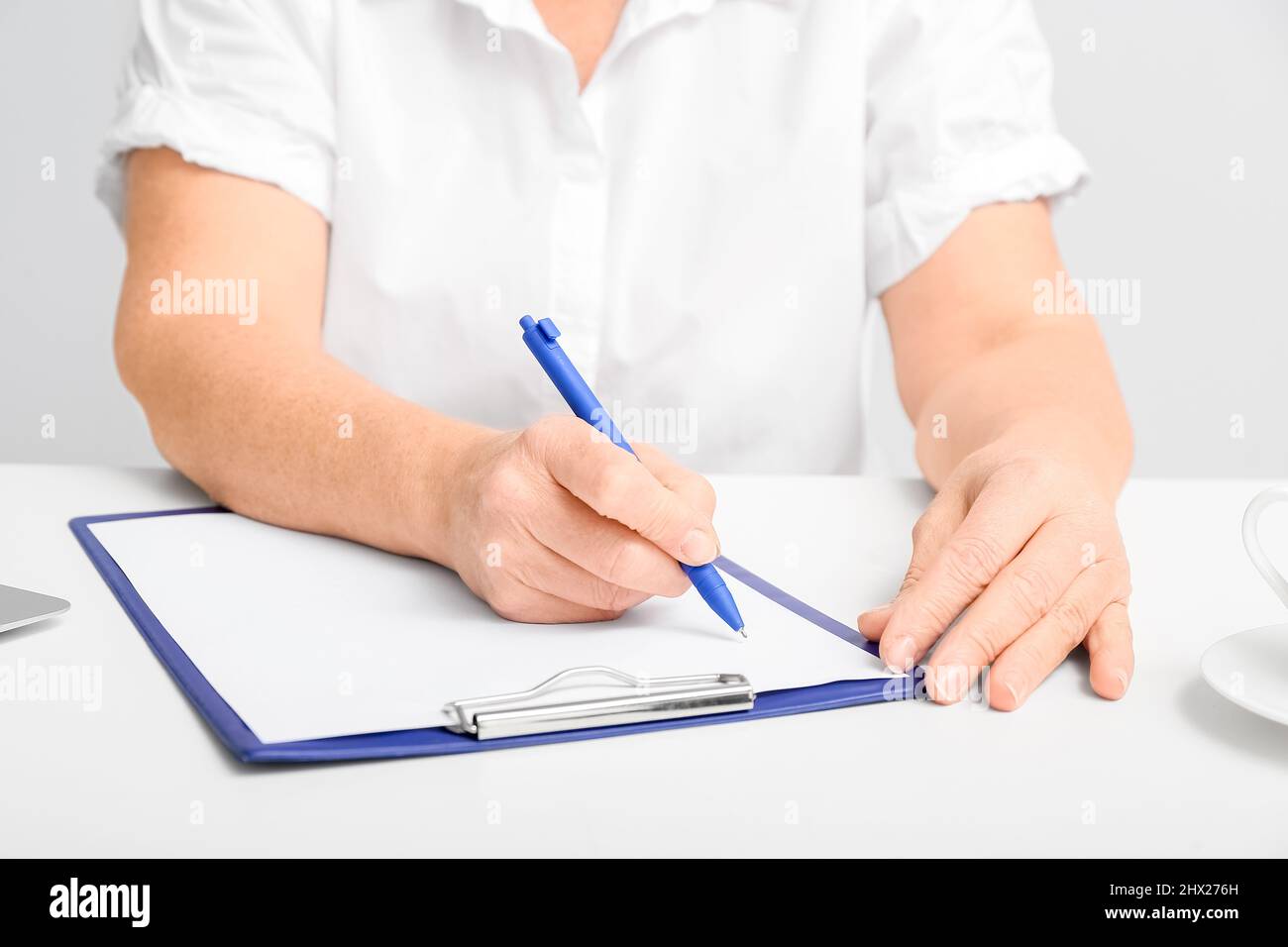 Mature secretary writing on clipboard at table on light background ...