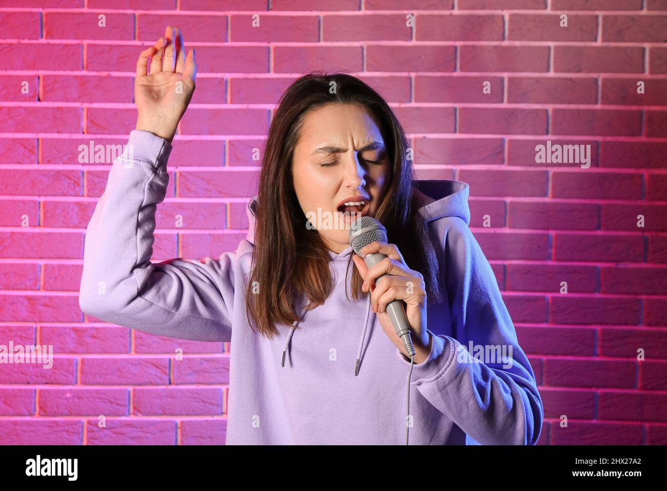 Cool young woman singing on color brick background Stock Photo - Alamy