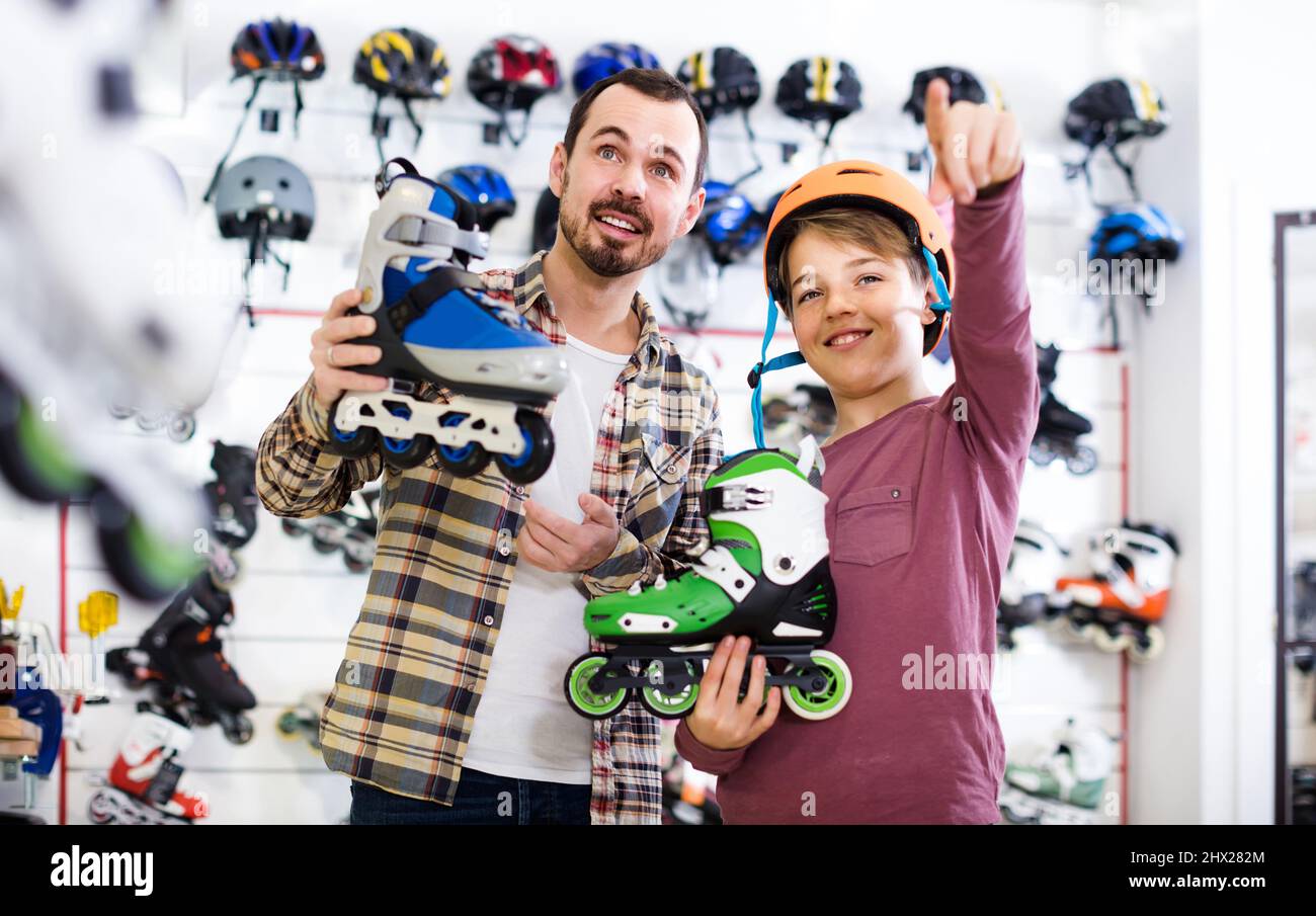 Male shop assistant helping boy to choose roller-skates in sports store ...