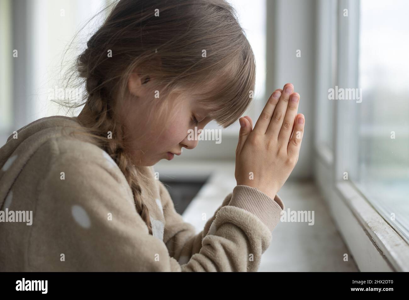 Praying little girl near window Stock Photo - Alamy