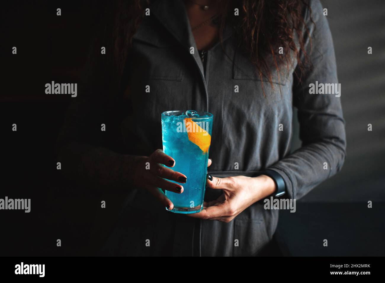 Woman holding blue cocktail in a highball with ice Stock Photo - Alamy