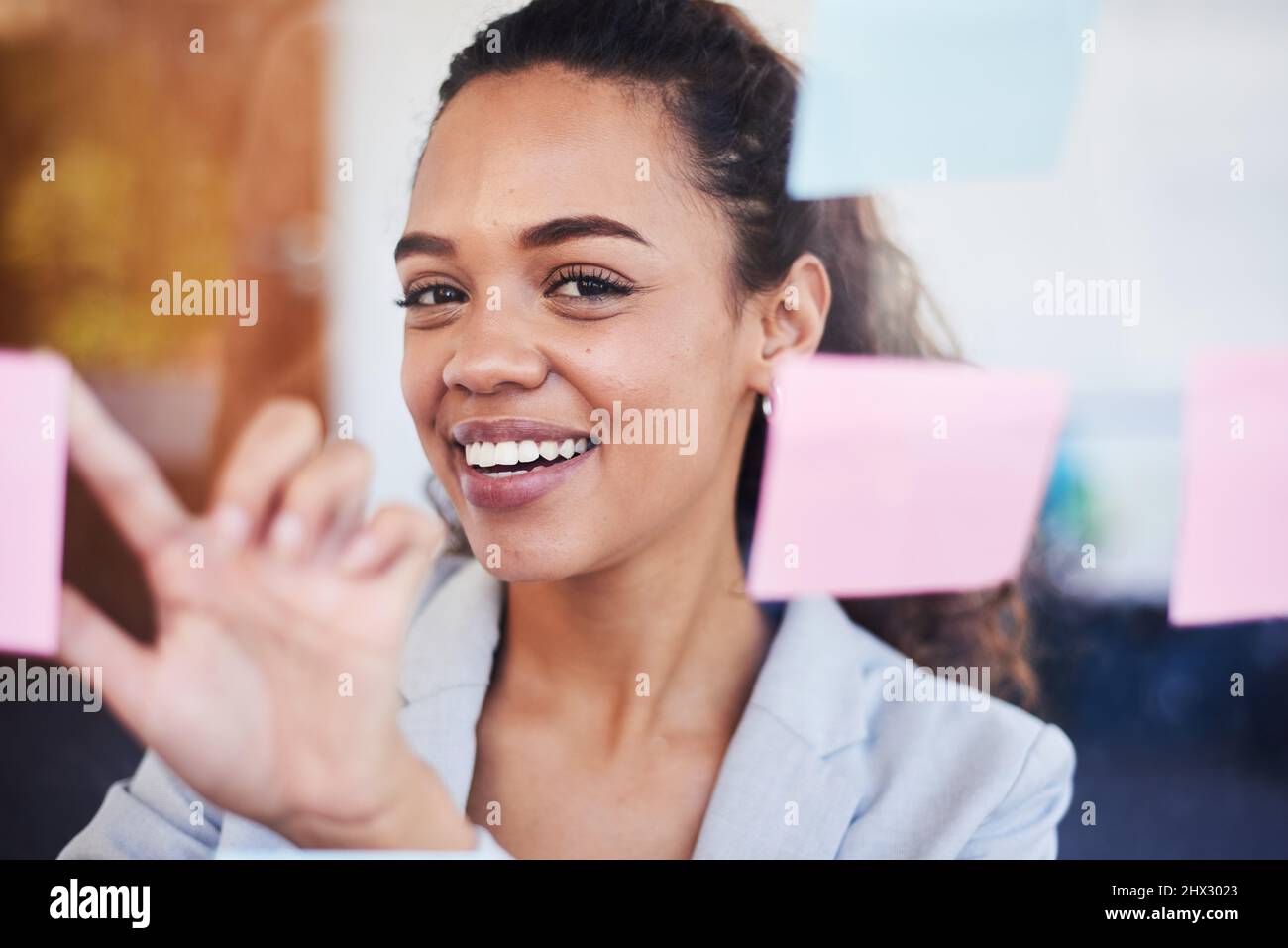 A young woman brainstorms ideas on sticky notes seen through window ...