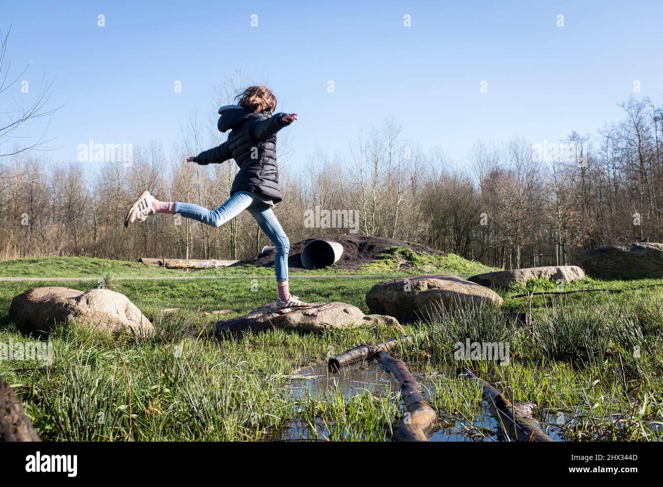 A young girl jumps dances over stones on an obstacle course in a park ...