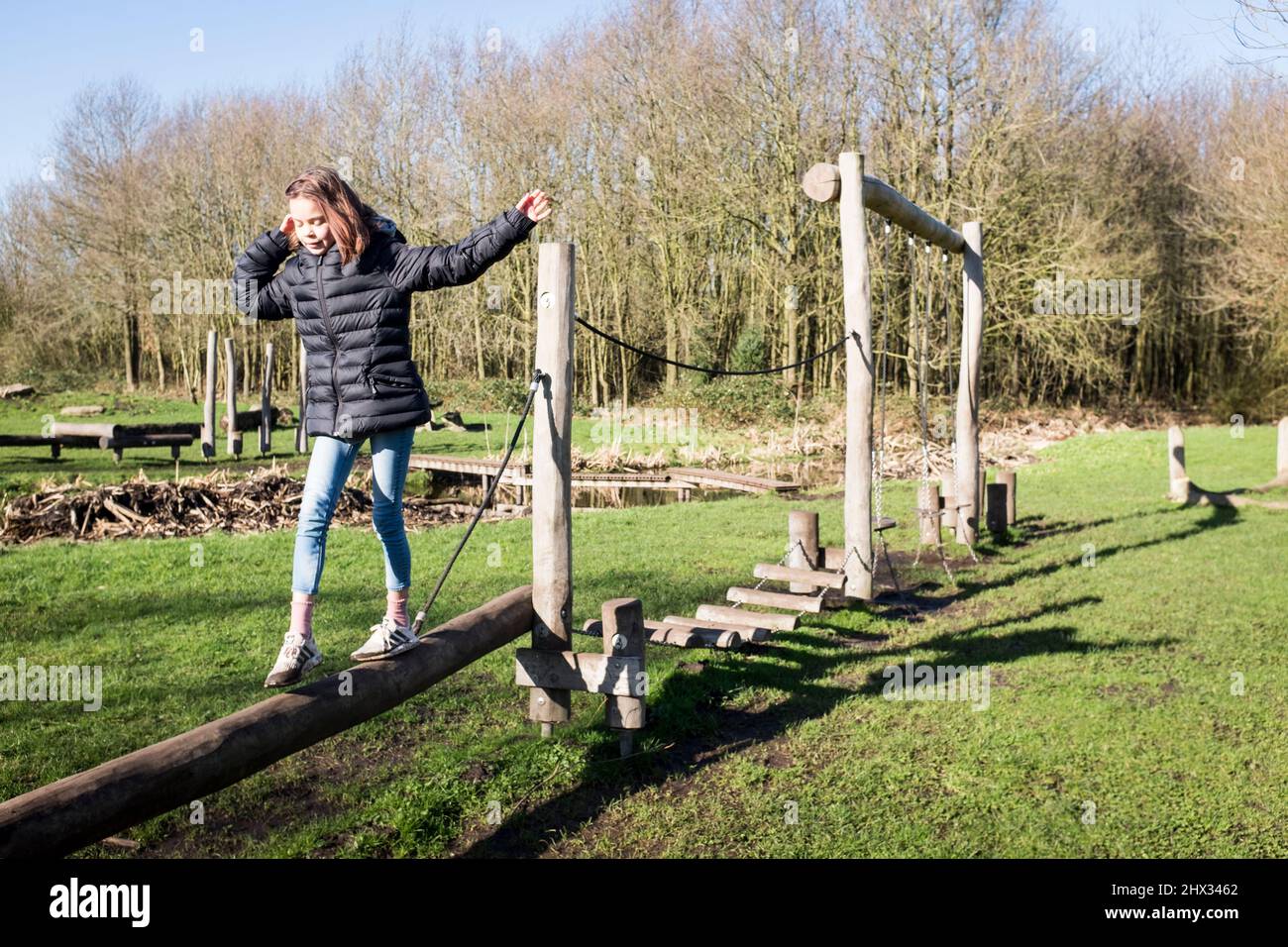 A young girl balances on a wooden beam on an obstacle course in a park ...
