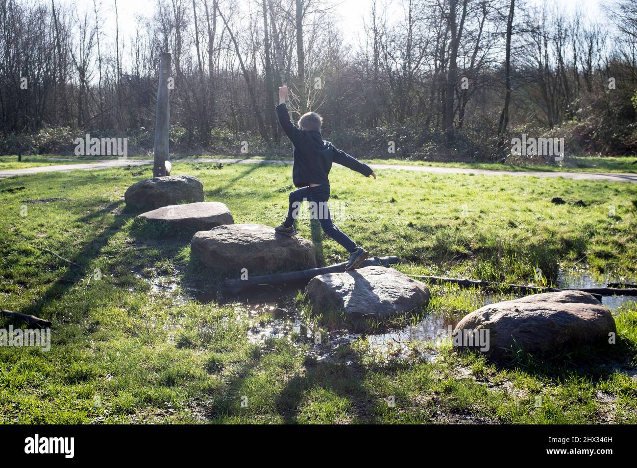A young boy jumps over stepping stones on an obstacle course in a park ...