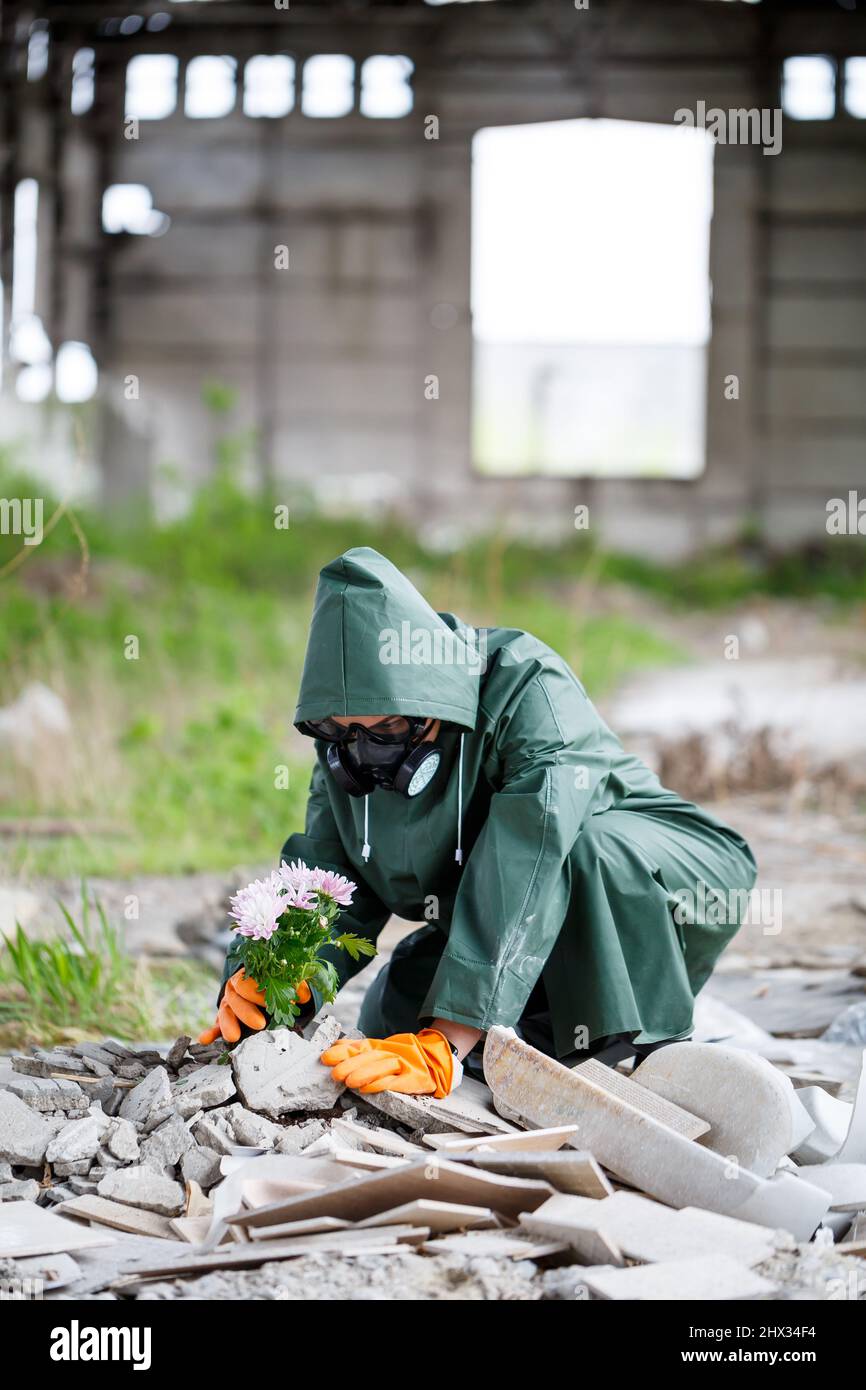 A man in a raincoat and gas mask collects a flower from a scorched ...