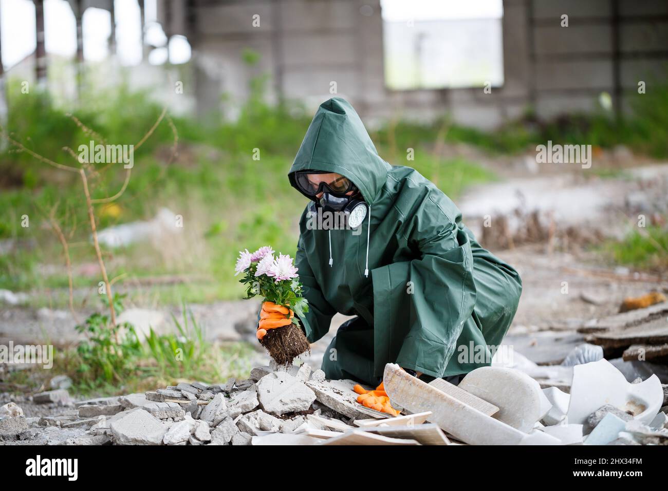 A man in a raincoat and gas mask collects a flower from a scorched ...