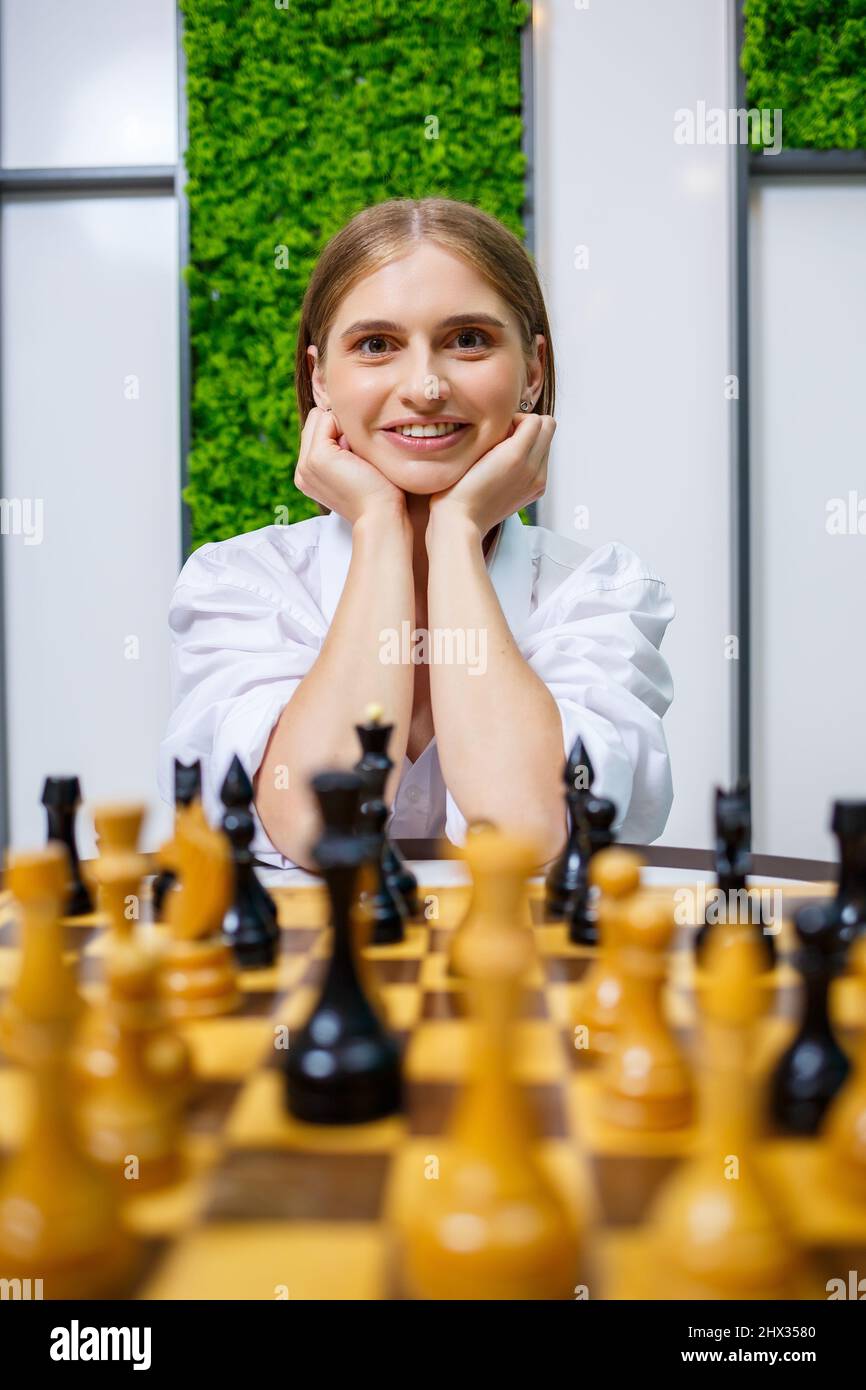 Young beautiful woman in a white shirt plays chess. Chess board with ...