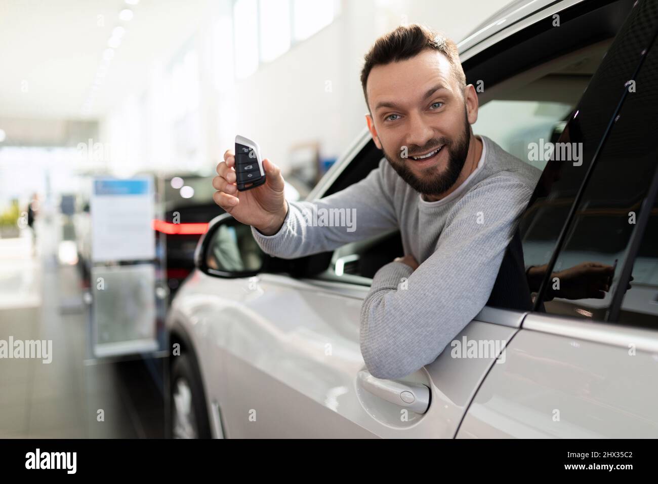 satisfied buyer of a new car with keys in his hands looking at the ...