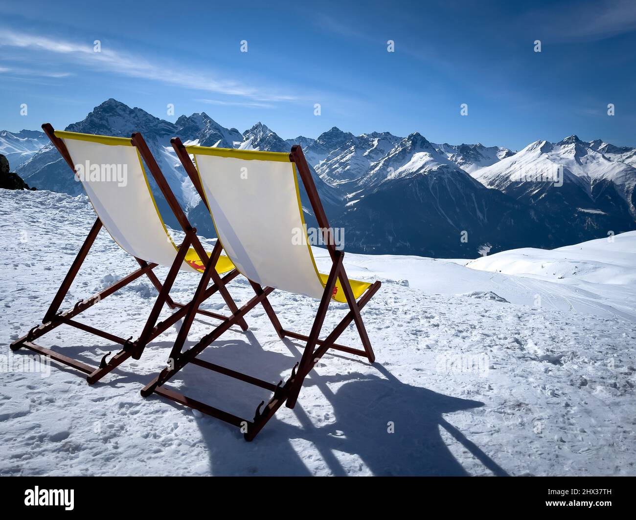 two yellow deck chairs are on the snow and in the background are the ...