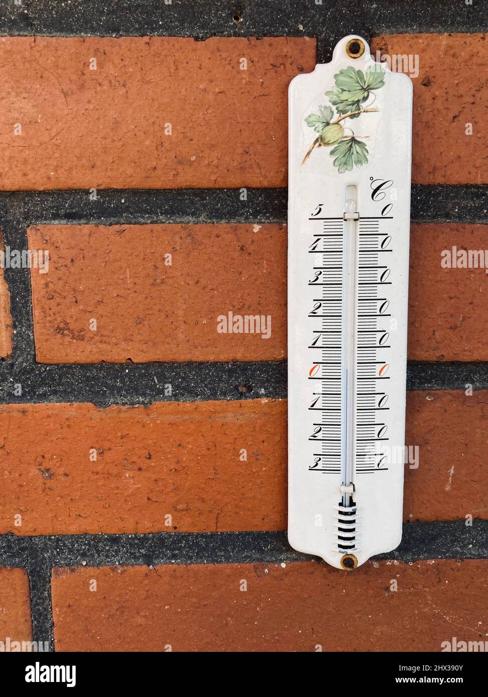 a white column thermometer with celsius scale hangs on a red brick wall ...