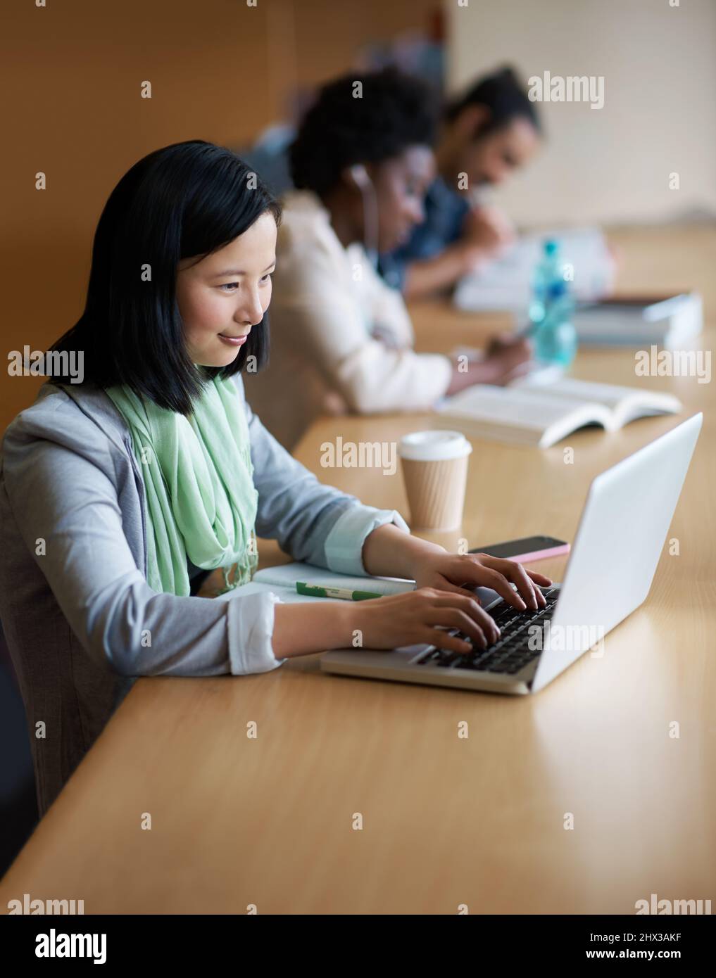 Working on her assignment. A young woman on a laptop in the library ...