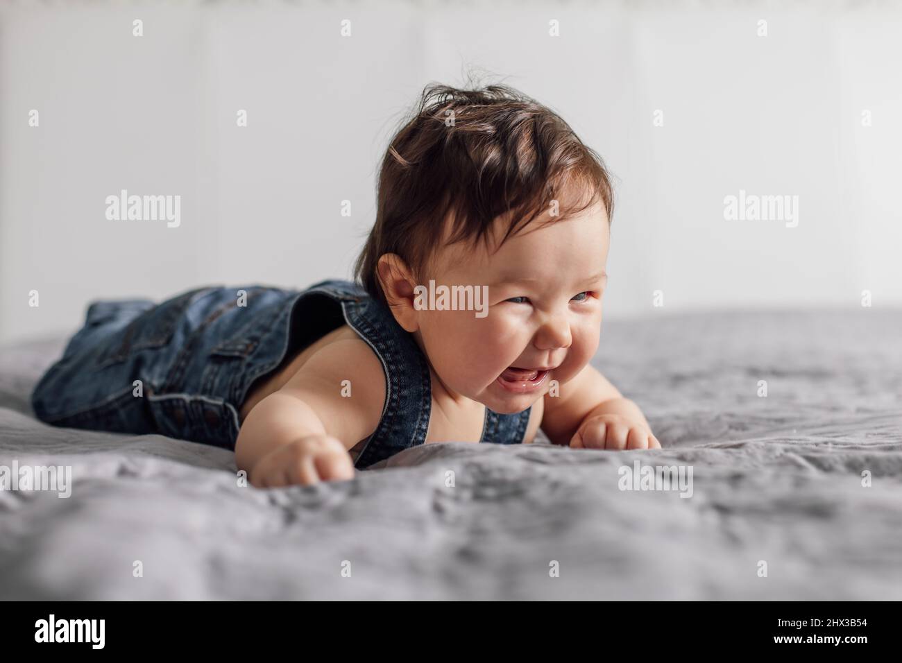 Portrait of pretty baby wearing denim romper lying on gray blanket at ... Portrait of pretty baby wearing denim romper lying on gray blanket at ...