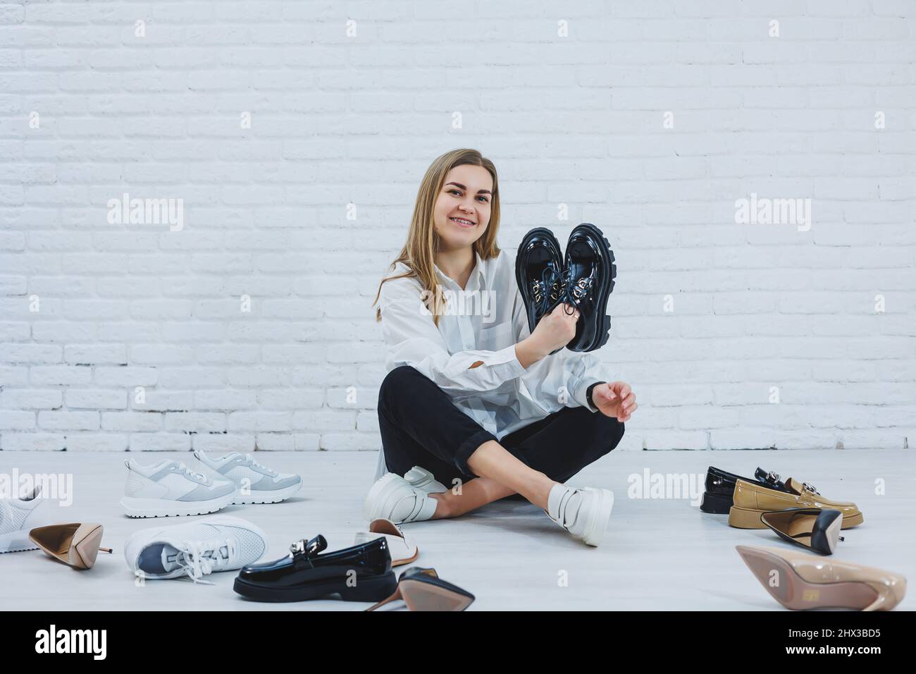 Stylish blonde choosing shoes while sitting on the floor. Side view of ...