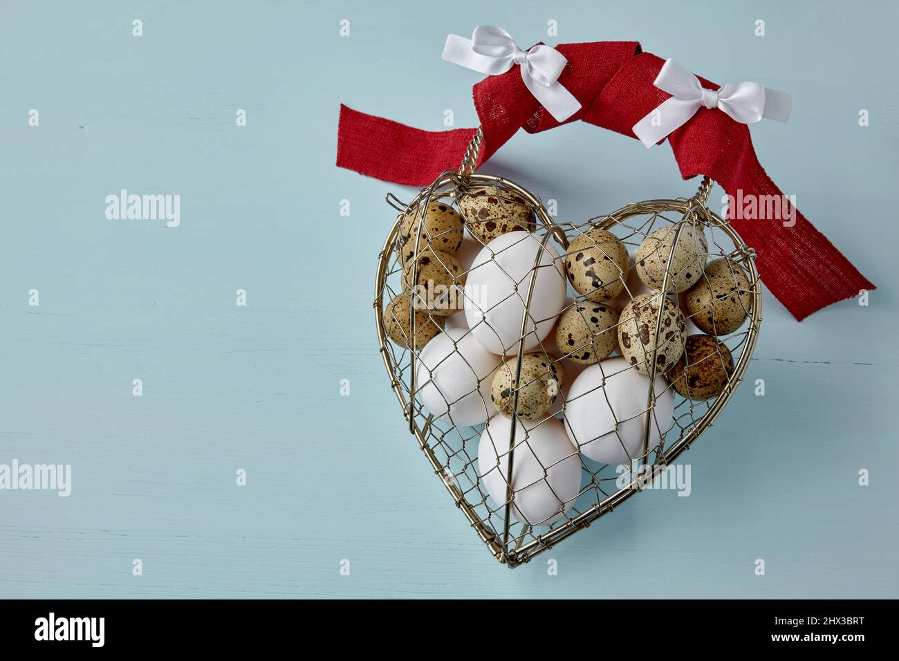Chicken and quail eggs in a heart shaped woven metal wire box tied ...