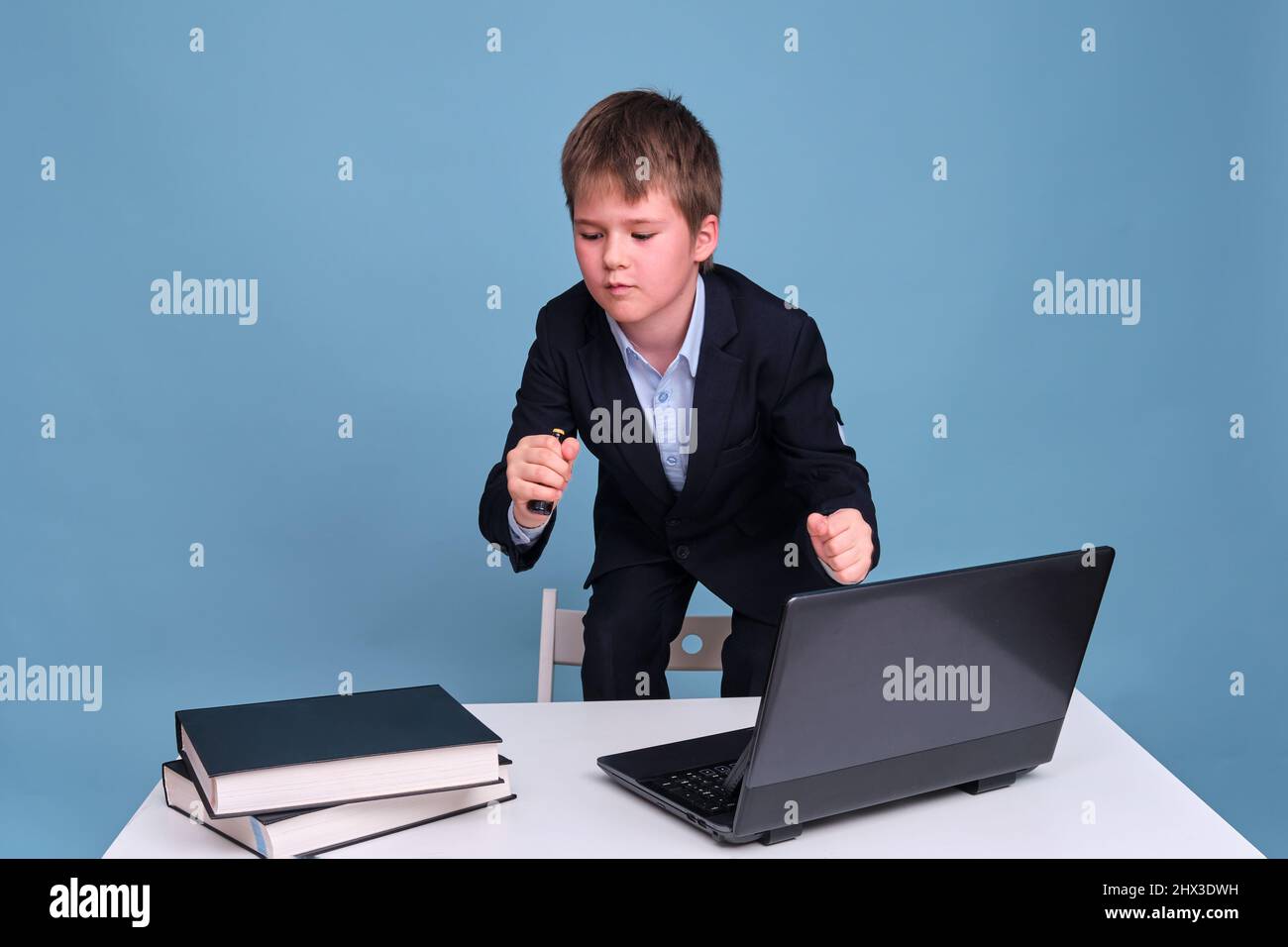 A boy in a school suit with dancing on a chair during distance learning ...