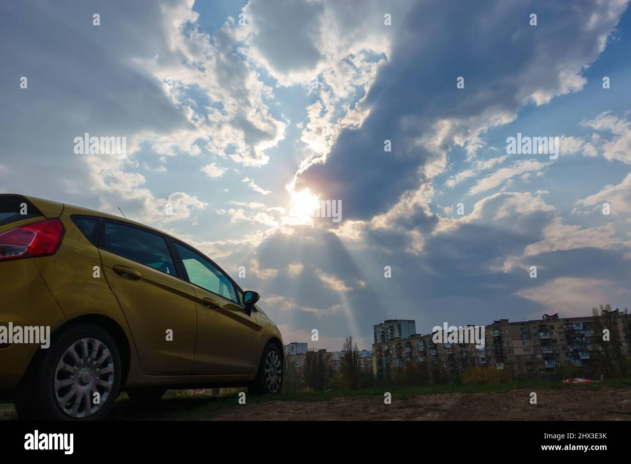 Yellow car on a background of epic sky. Rays of the sun in the cloudy ...