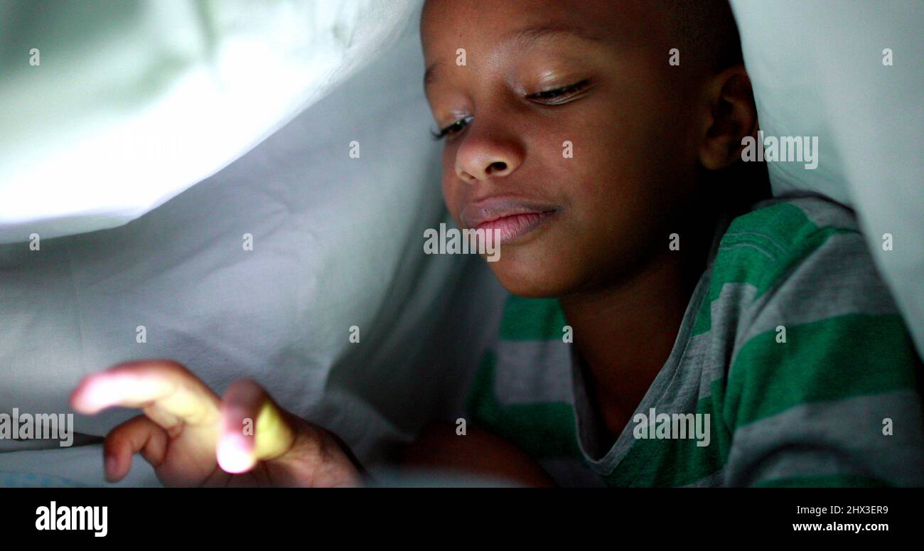 African child using smartphone at night under blanket, mixed race kid ...