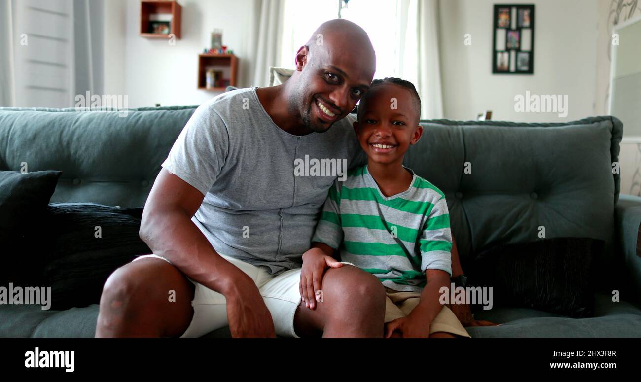 African father and son sitting on couch smiling at camera Stock Photo ...