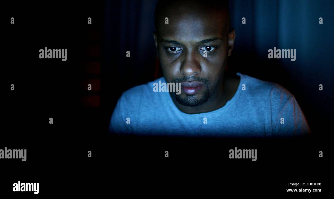 African man browsing internet at night in the dark. Black person ...