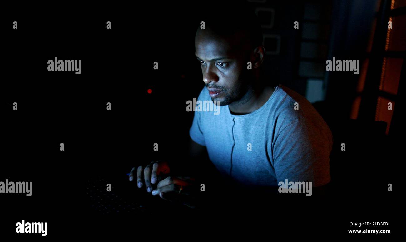 African man looking at laptop screen at night in the dark, person ...