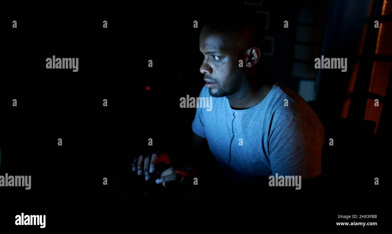 African man looking at laptop screen at night in the dark, person ...