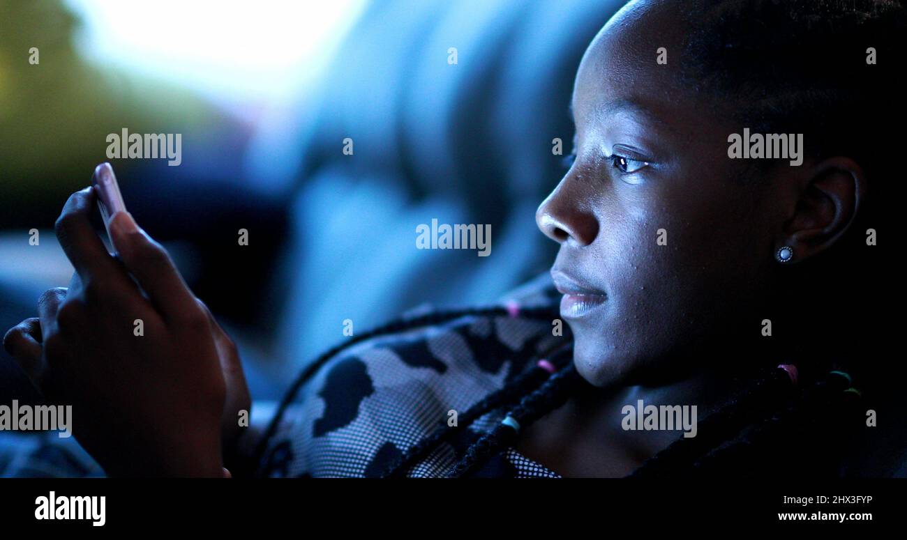 African teen girl looking at cellphone screen in the dark at night ...