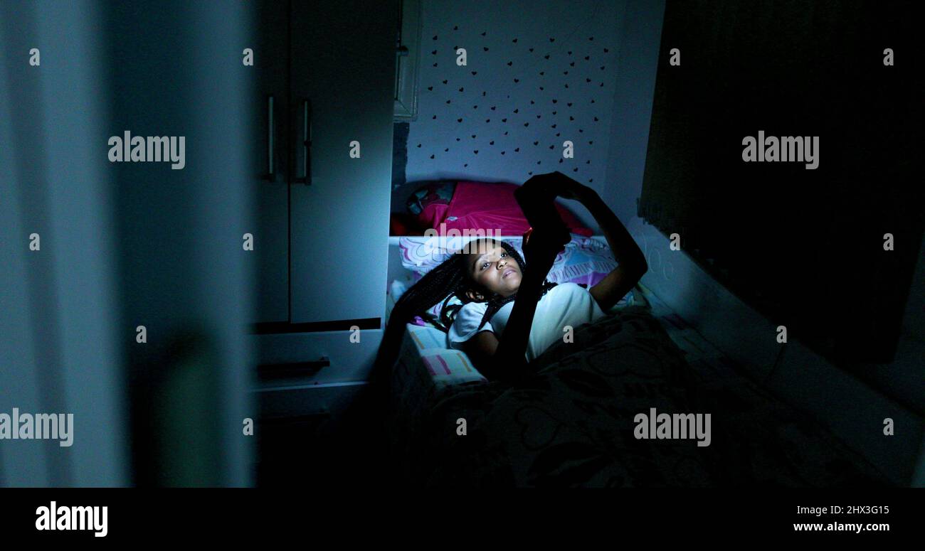 African teen girl looking at cellphone screen in the dark at night ...
