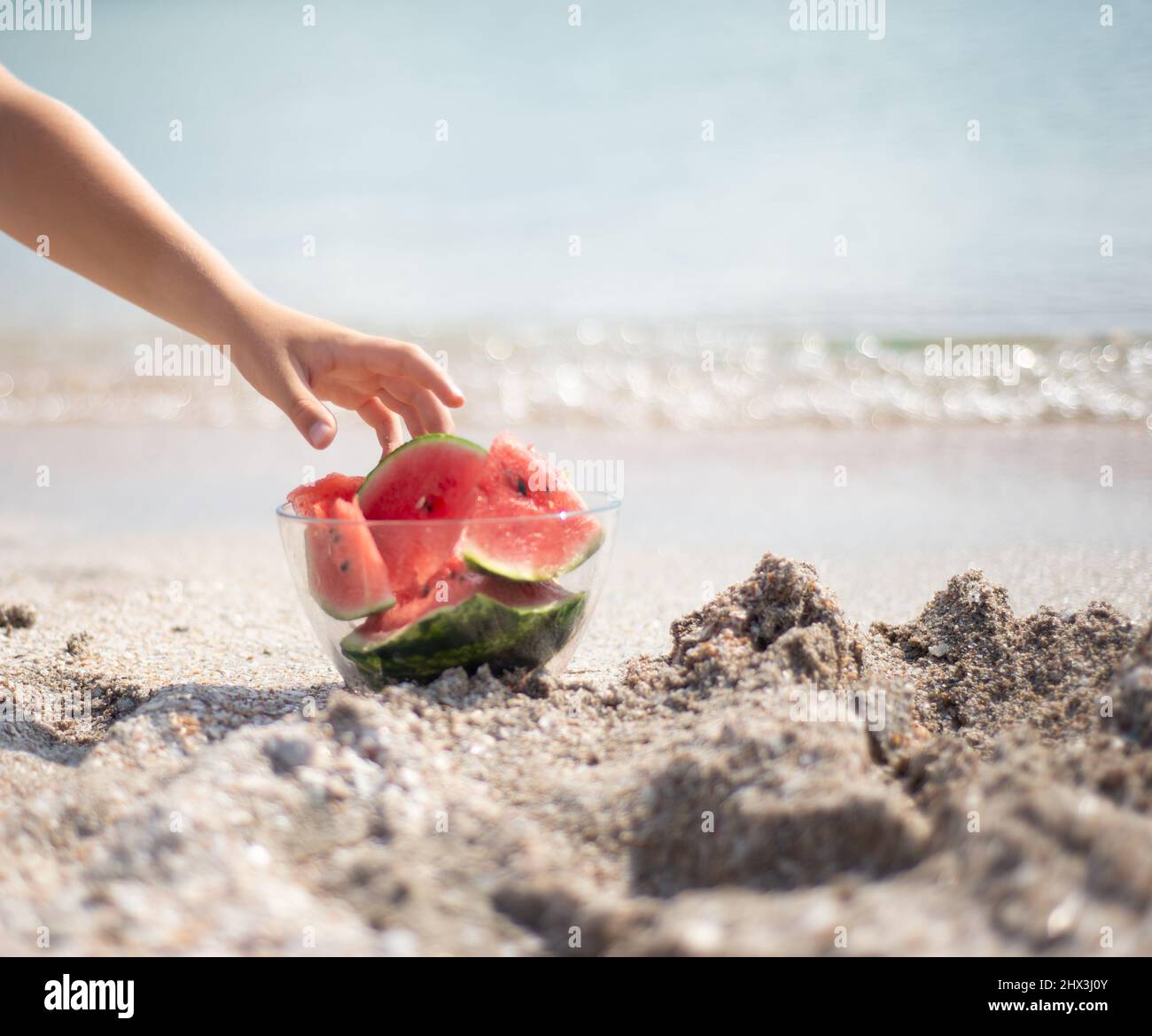 Glass transparent bowl with watermelon slices on the beach. The hand ...