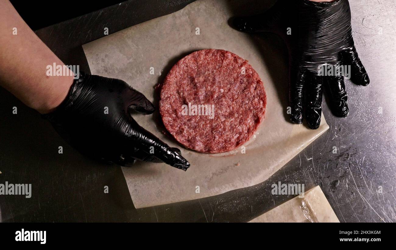Cook makes meat medallions for burgers. Chef in black food gloves makes ...