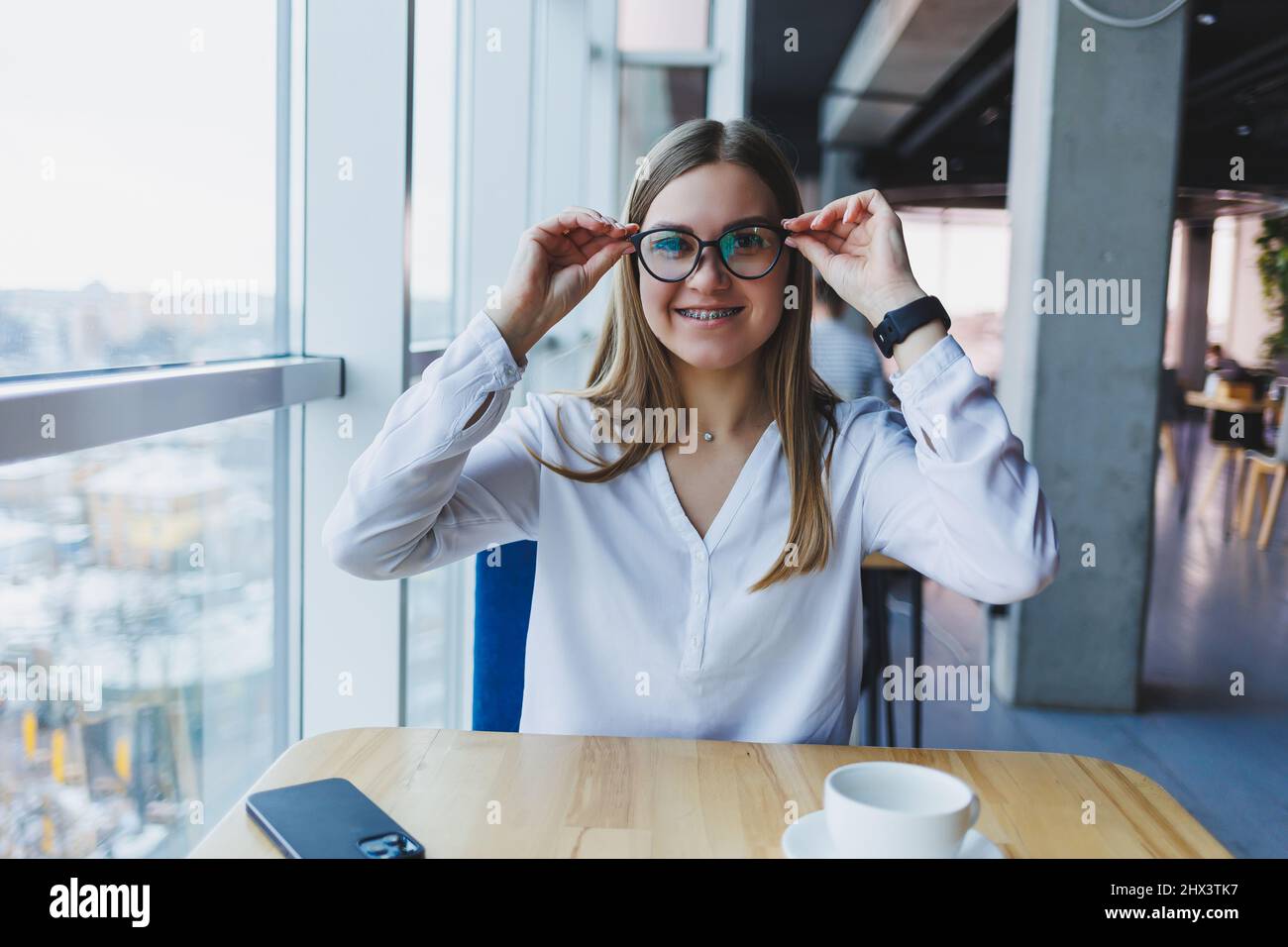 A young female manager puts on glasses and gets to work, she is sitting ...