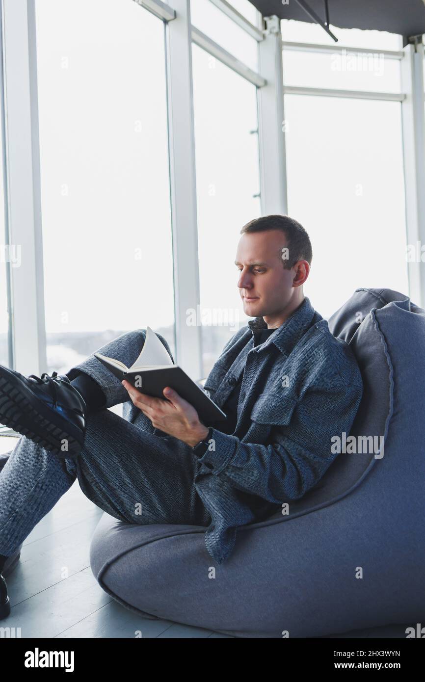 A male businessman in a casual suit resting in a comfortable pouf while ...